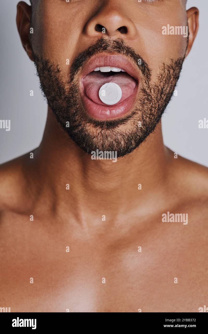 Man, mouth and pill on tongue in studio for substance abuse, narcotics ...