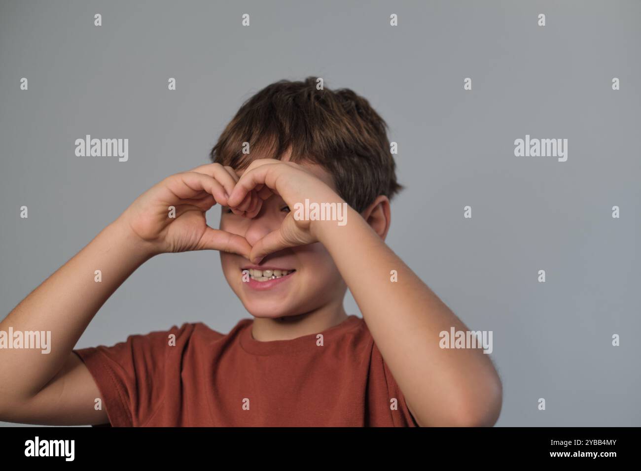 Smiling child makes a heart shape with his hands, eyes gleaming with ...