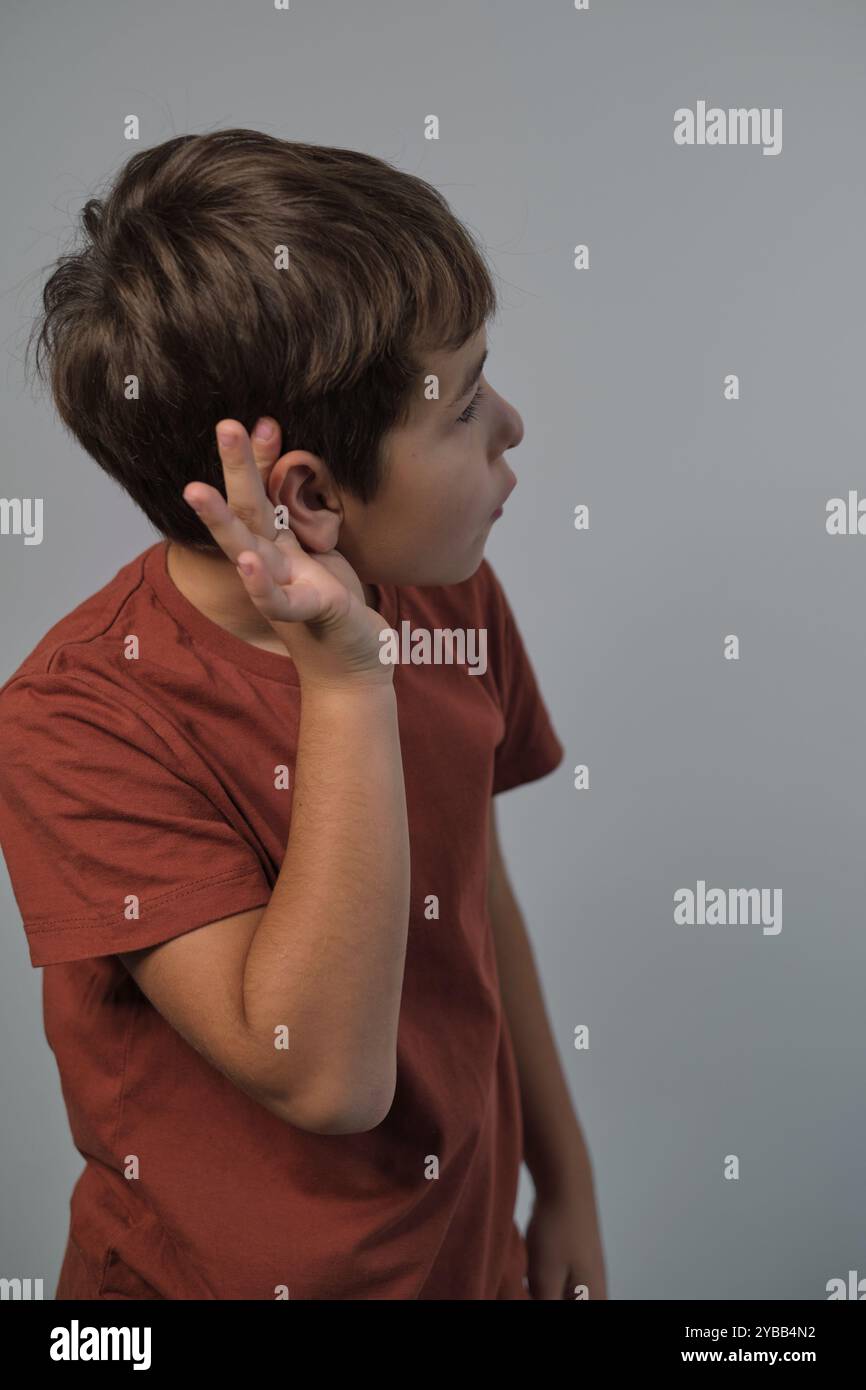 boy attentively listens, hand to ear, a gesture of focus. This image ...