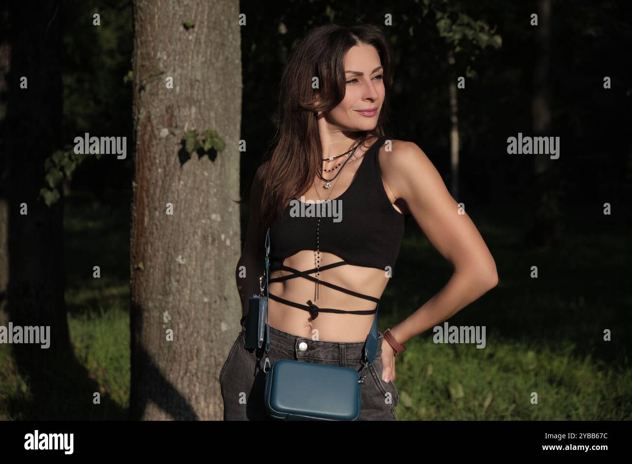 Woman standing in a sunlit forest, wearing a black top and jeans ...