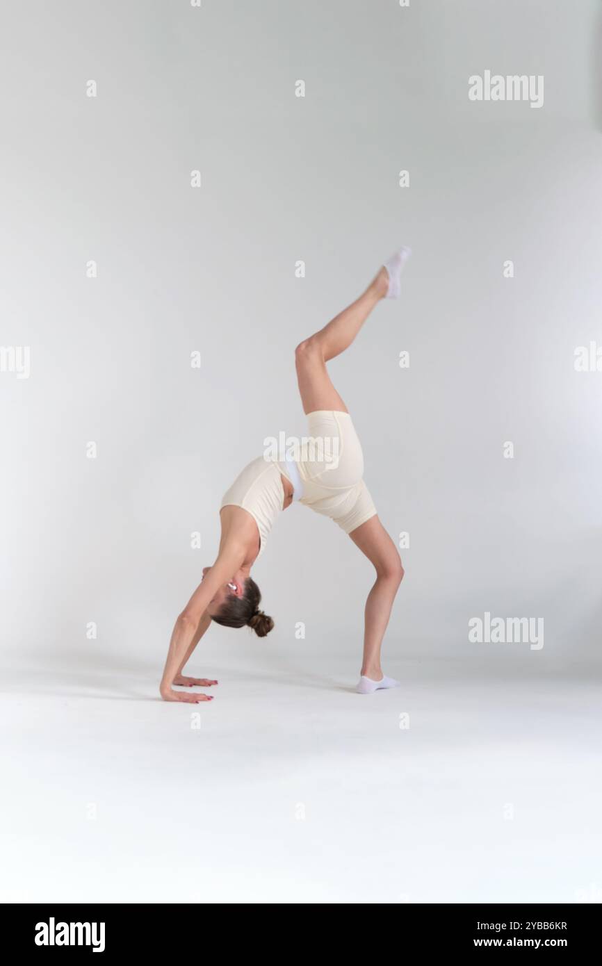 Female in an elegant beige workout ensemble, lifting her leg high in a ...