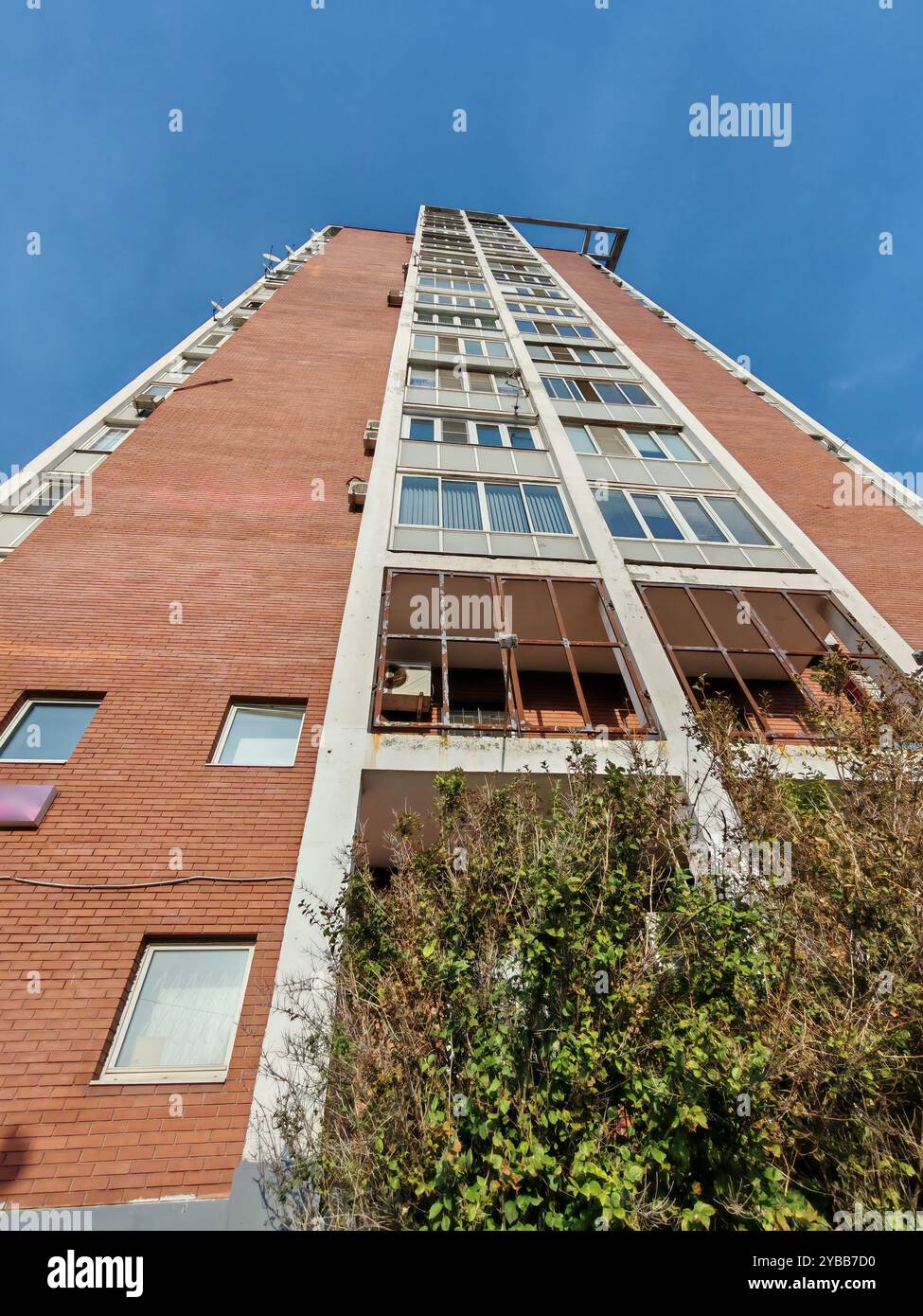 A tall red and beige brick residential building with multiple balconies ...