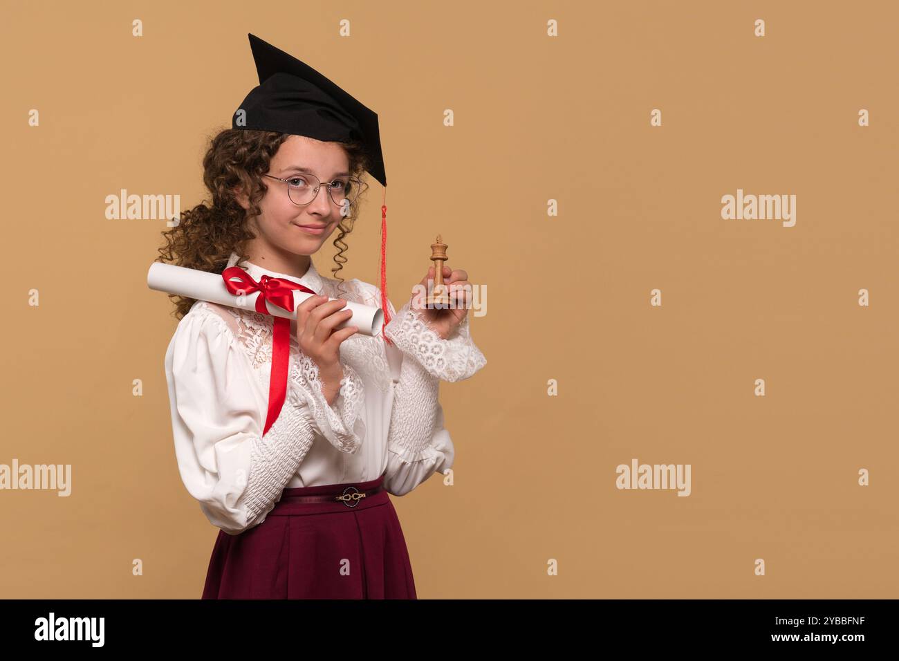 A young graduate in cap and gown proudly holding a diploma scroll and a ...