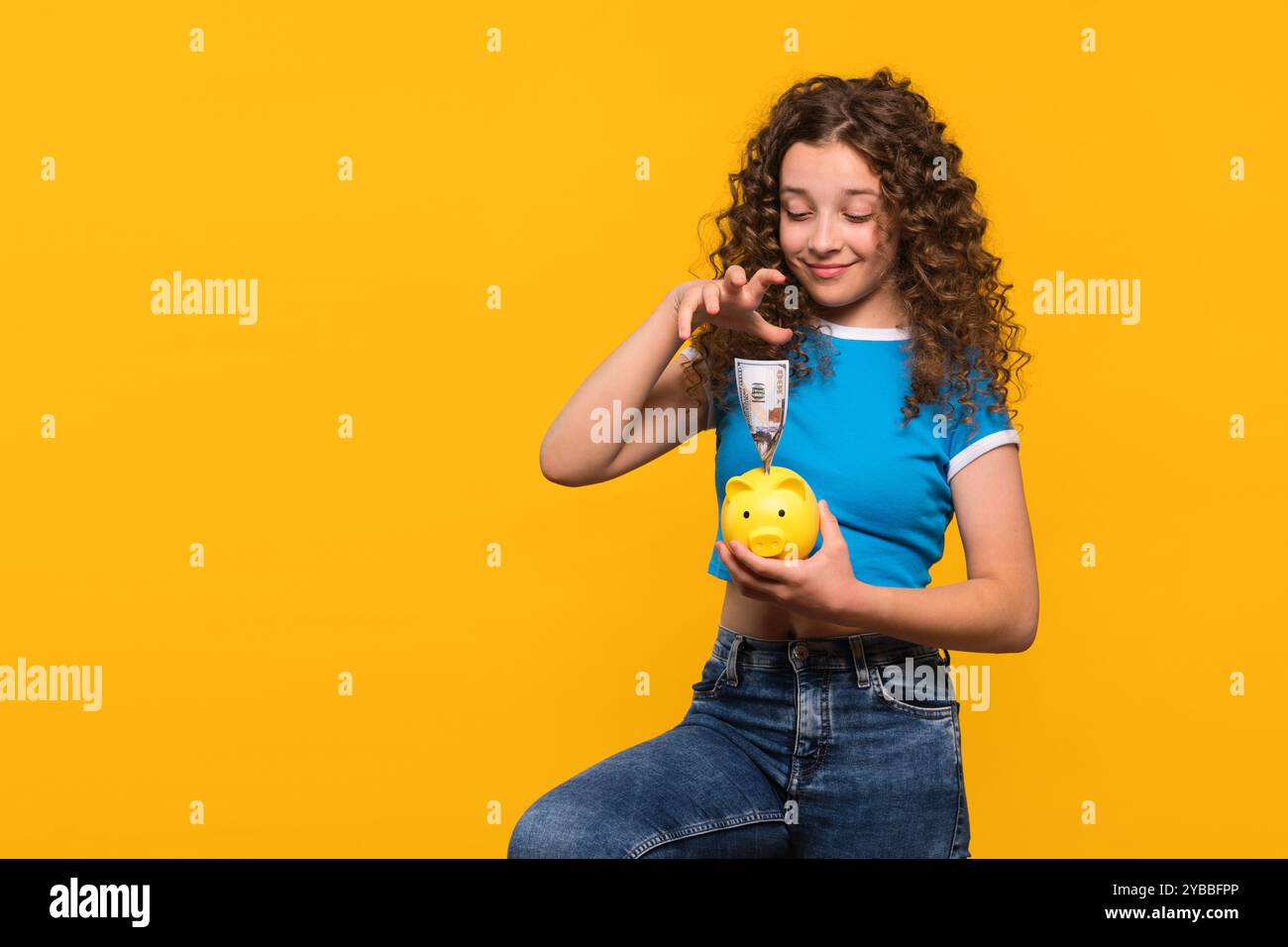 Girl smiling as she saves money in a piggy bank, demonstrating ...
