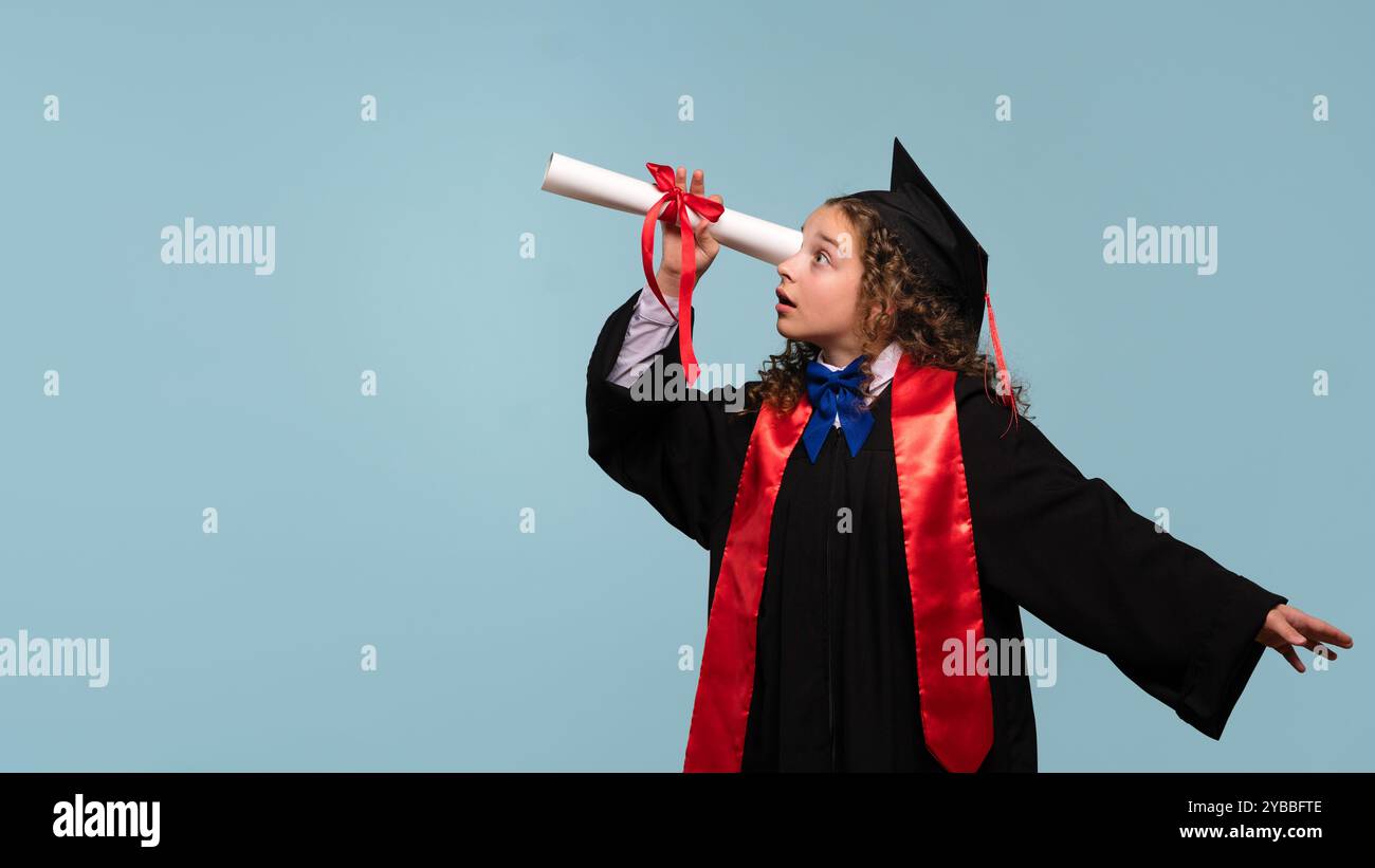 Young girl in graduation attire looking through diploma like a ...