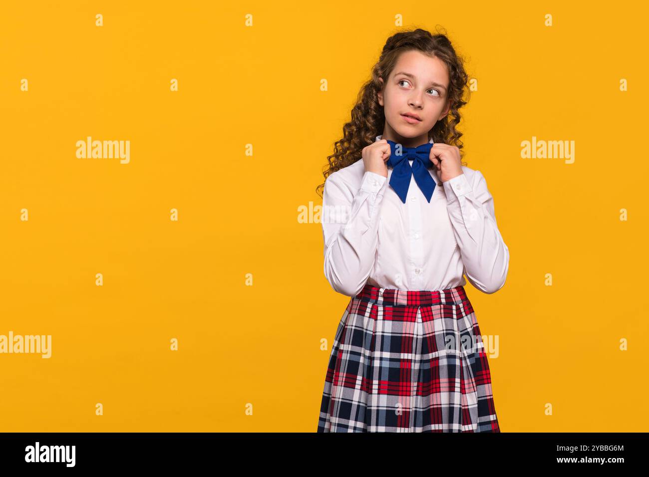 Girl adjusting blue bowtie, thoughtful expression, plaid skirt Stock ...