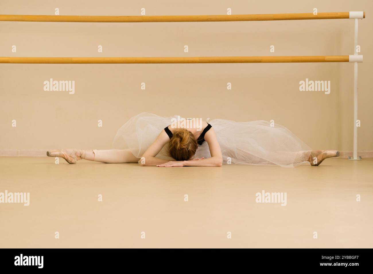 A ballet dancer stretches forward on the studio floor, showcasing ...