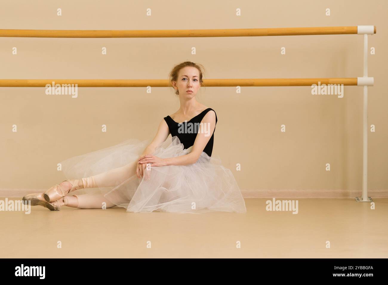 A ballet dancer sits on the floor in a dance studio, demonstrating ...