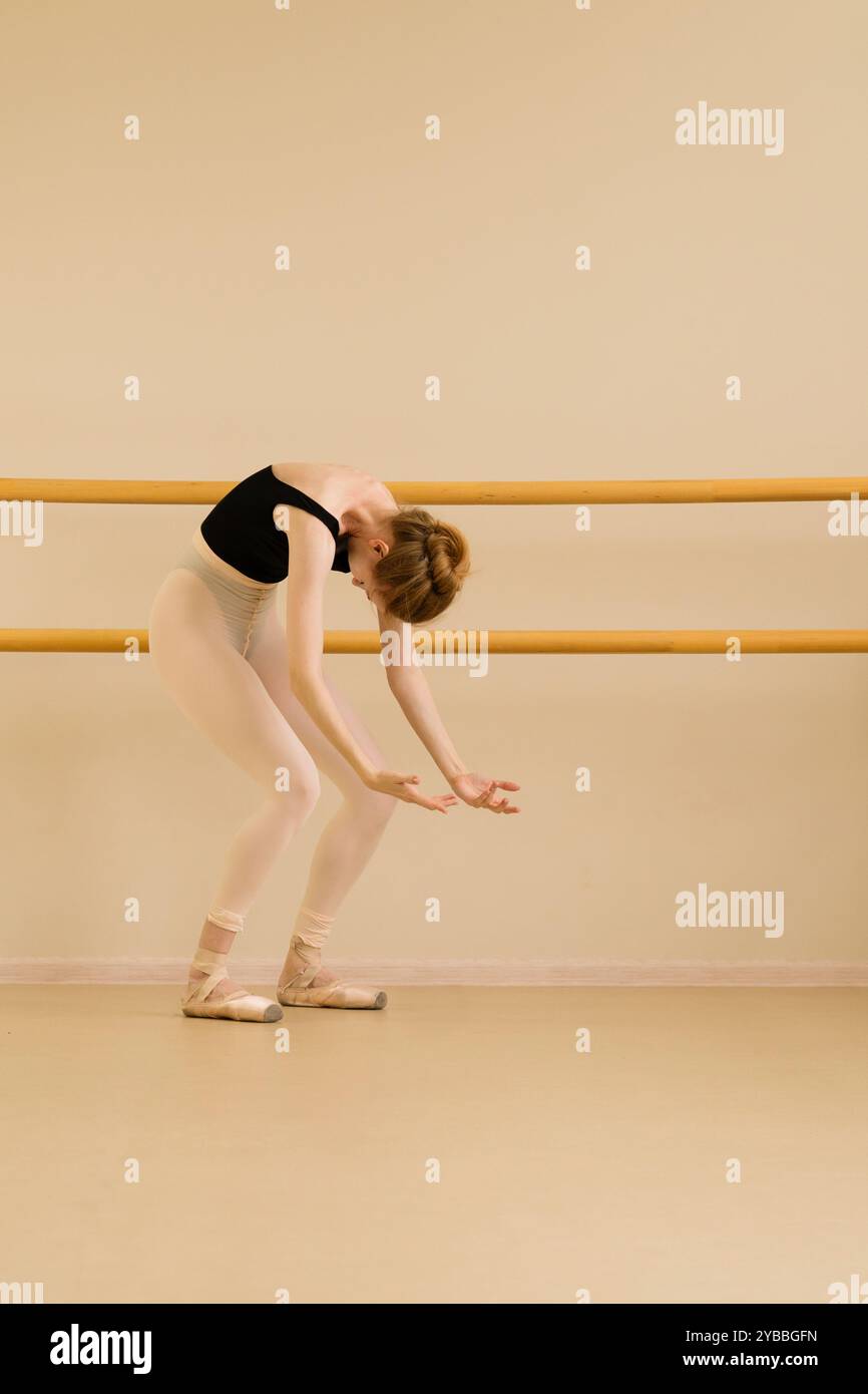 Ballet dancer bending forward at the barre, extending her arms in a ...