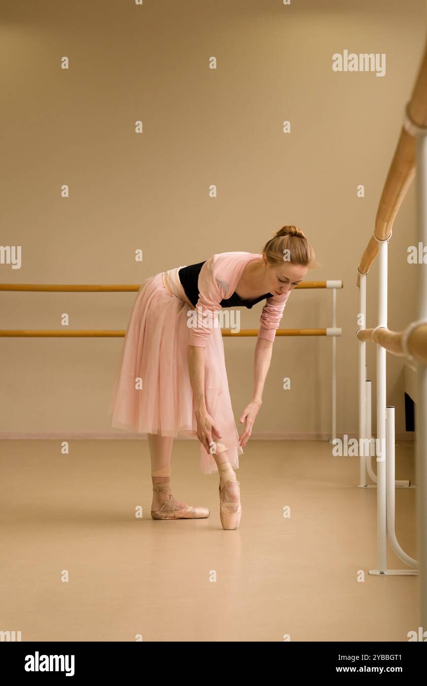 Ballet dancer bending down to adjust pointe shoe during practice Stock ...