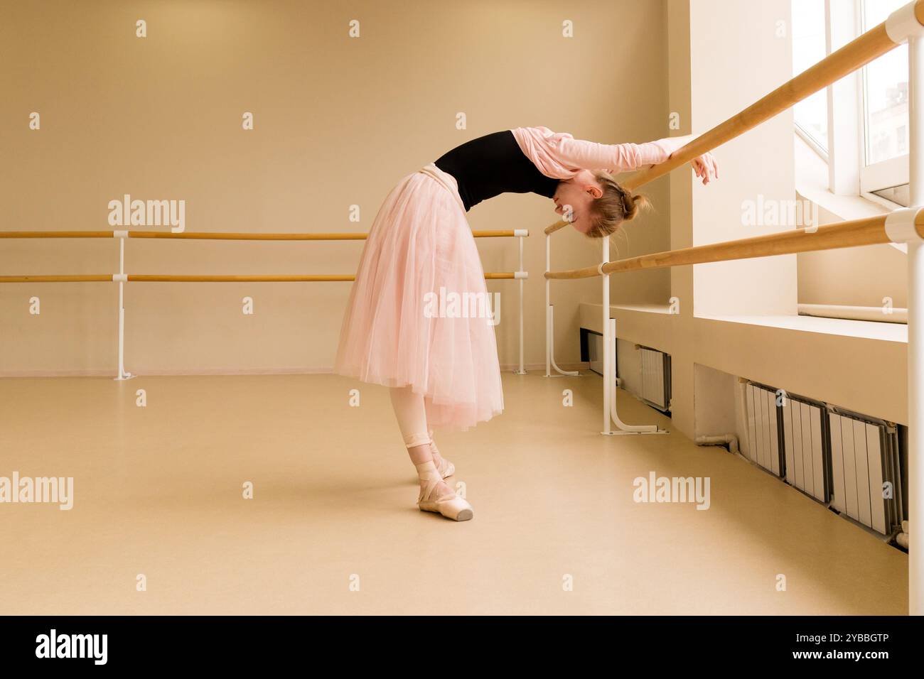 Ballet dancer arching backward at barre, dressed in pink tutu during ...