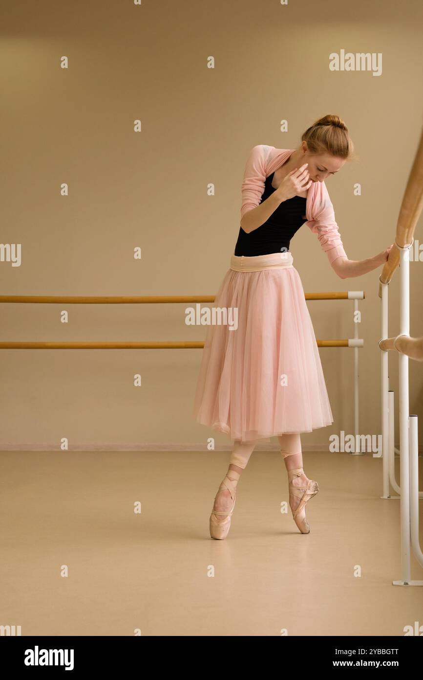 Ballet dancer resting her hand on the barre while standing en pointe in ...