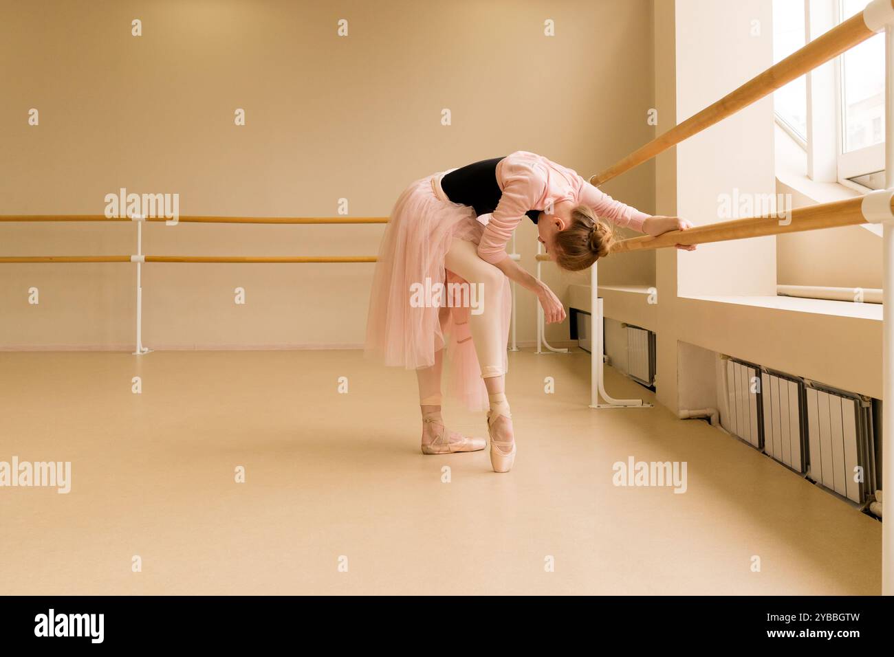 Ballet dancer leaning on barre, stretching in pink tutu and pointe ...