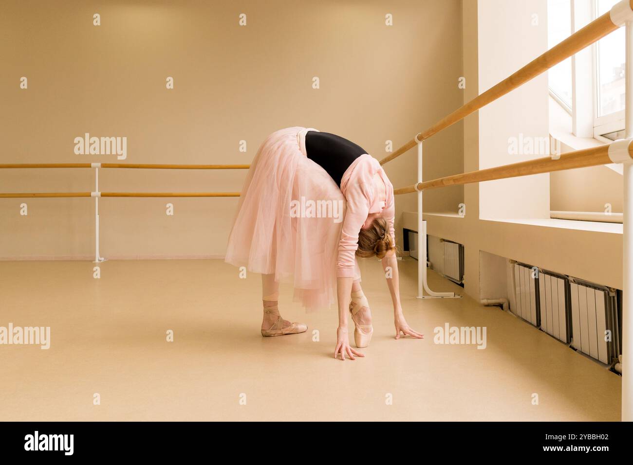 Ballet dancer bending forward in pink tutu, stretching at barre Stock ...