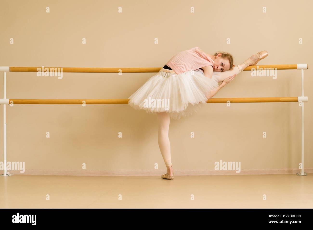 A ballet dancer rests on the barre, holding a stretch with her leg ...