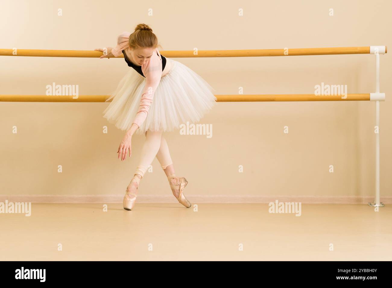 A ballet dancer balances on pointe, stretching downward while extending ...