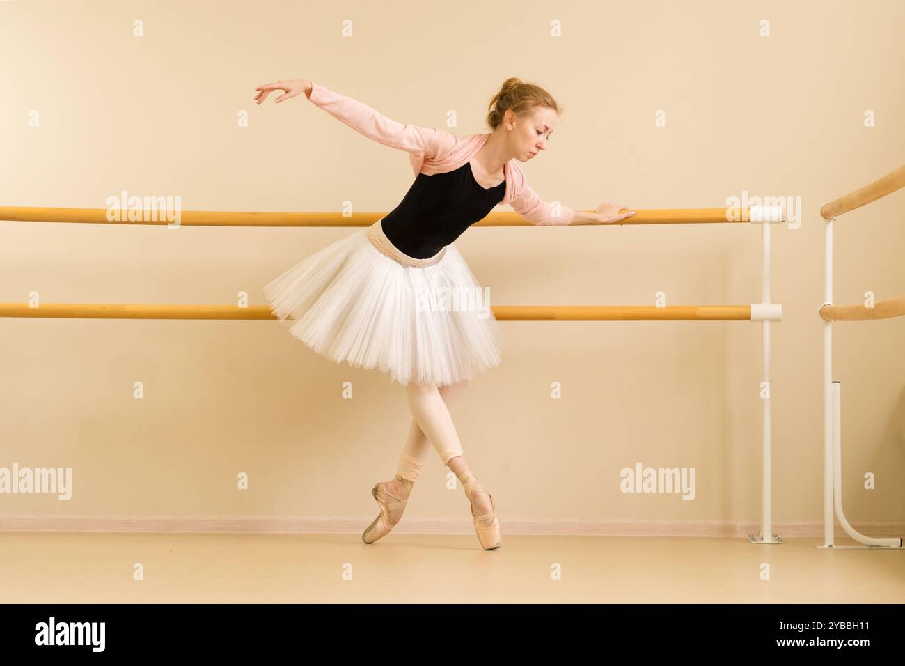 A ballet dancer stretches while holding the barre, balancing on pointe ...