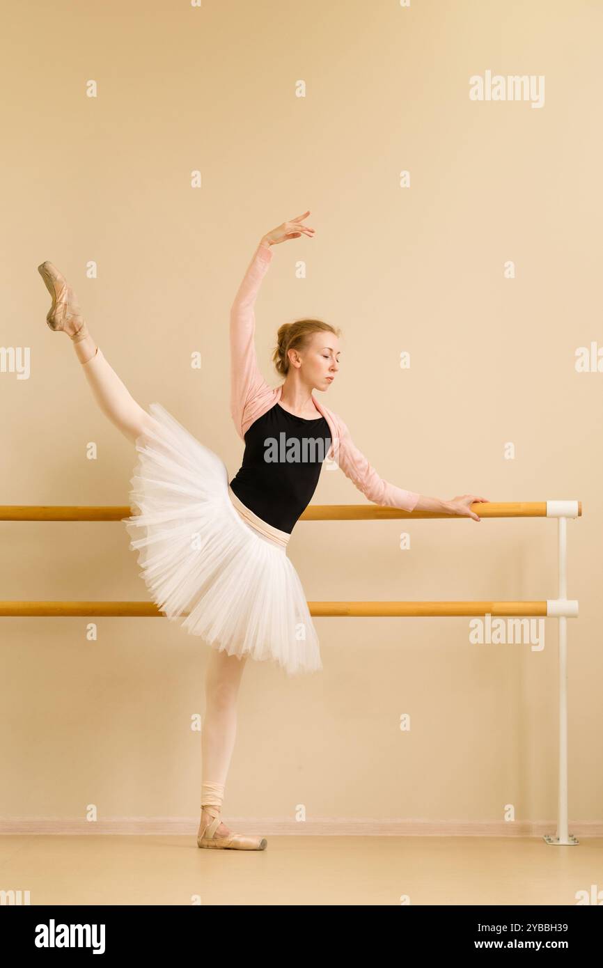 Ballet dancer practicing leg lift with graceful arm pose at barre Stock ...