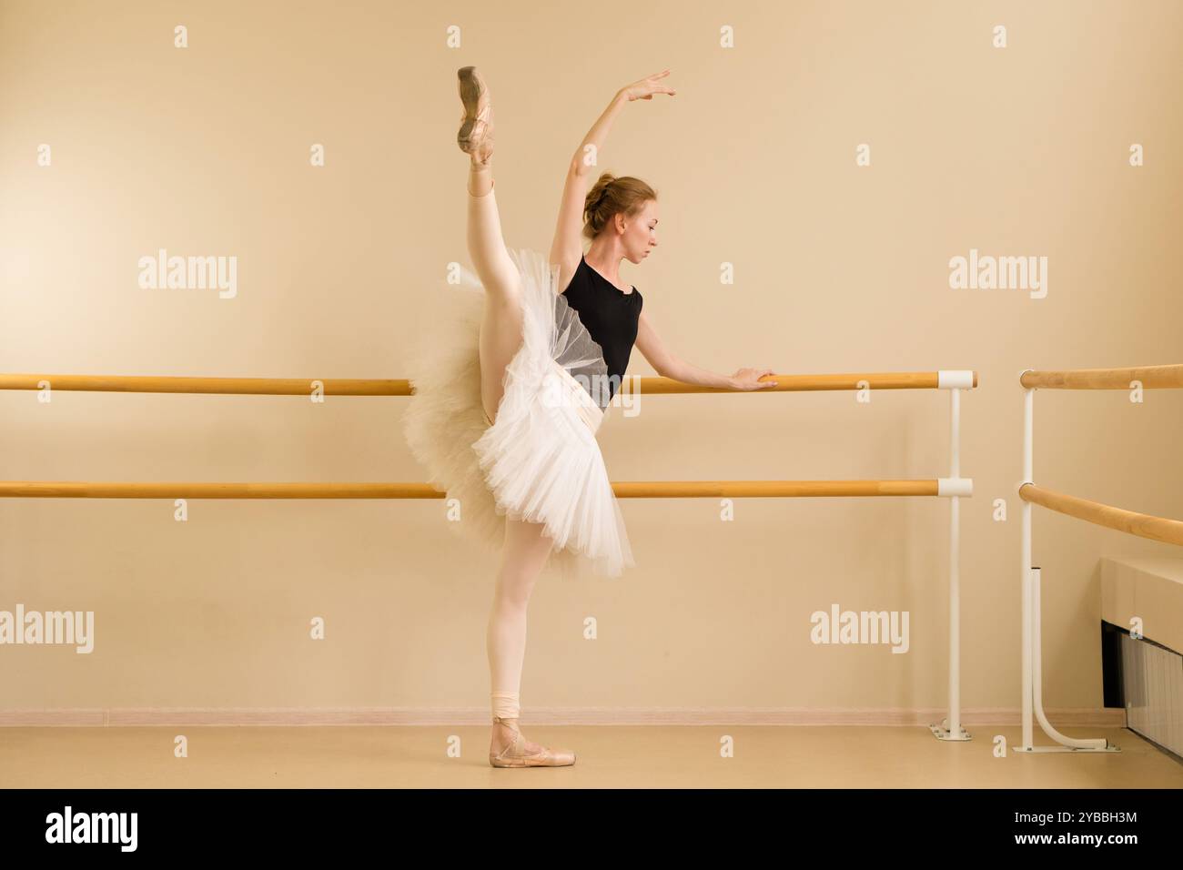 Ballet dancer performing a high leg extension at barre with elegant arm ...