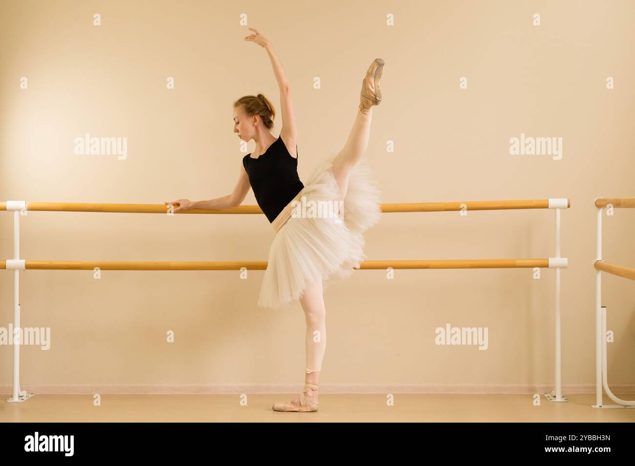 Ballet dancer holding pointe shoe in high leg extension at barre Stock ...