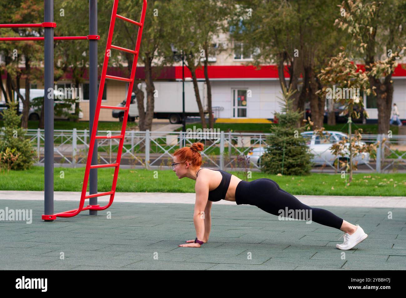 A woman doing a plank exercise next to a red fitness structure in an ...