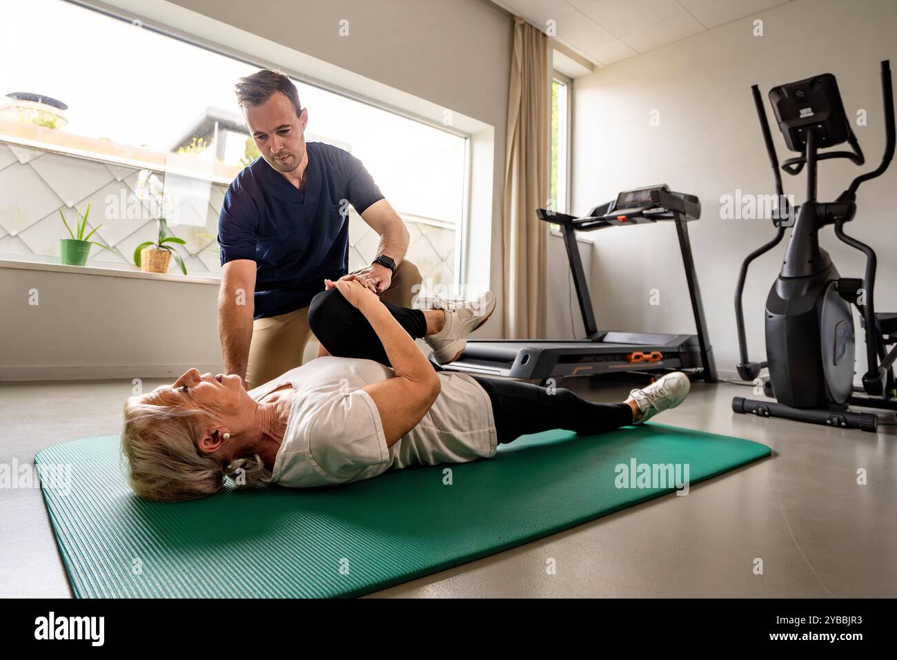 Male physiotherapist helping elderly female patient with knee mobility ...