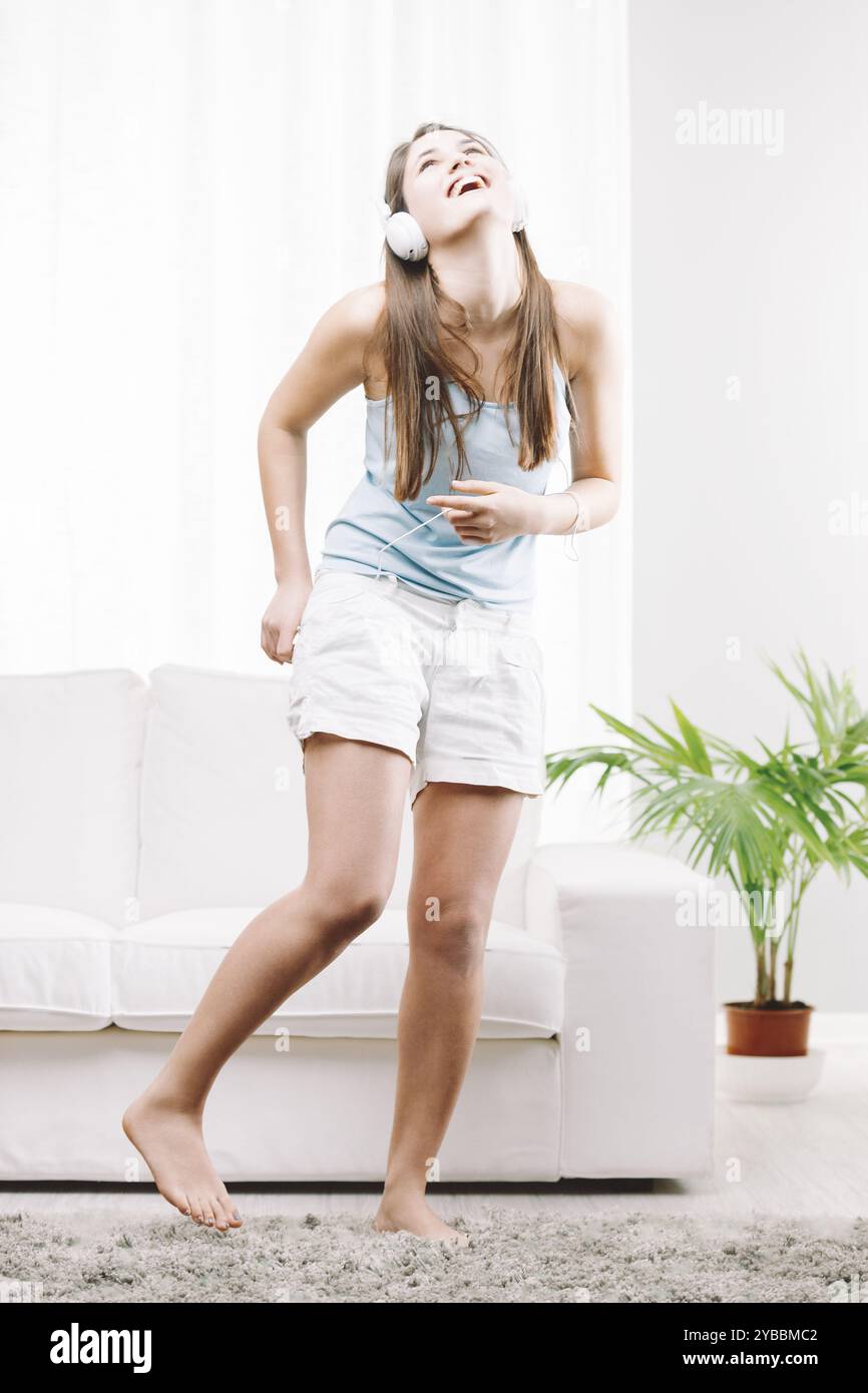 Carefree young woman dancing happily barefoot in her bright living room ...