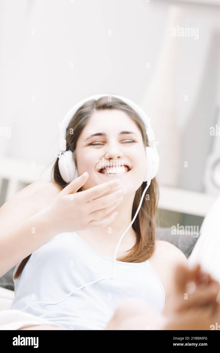 Joyful woman relaxes at home, listening to music on her smartphone with ...