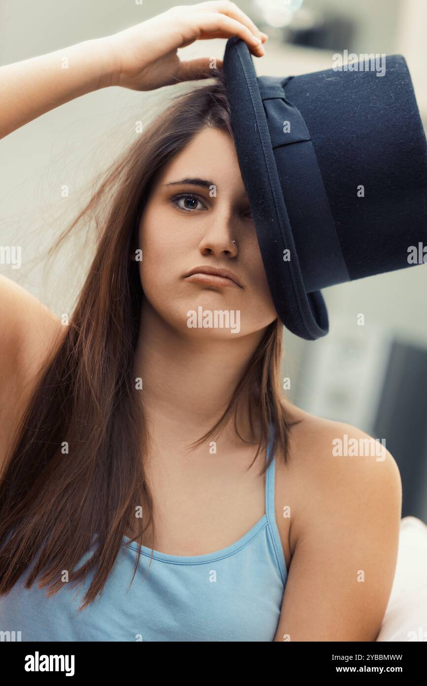 Young woman holds a black top hat over her face, looking bored. Her ...