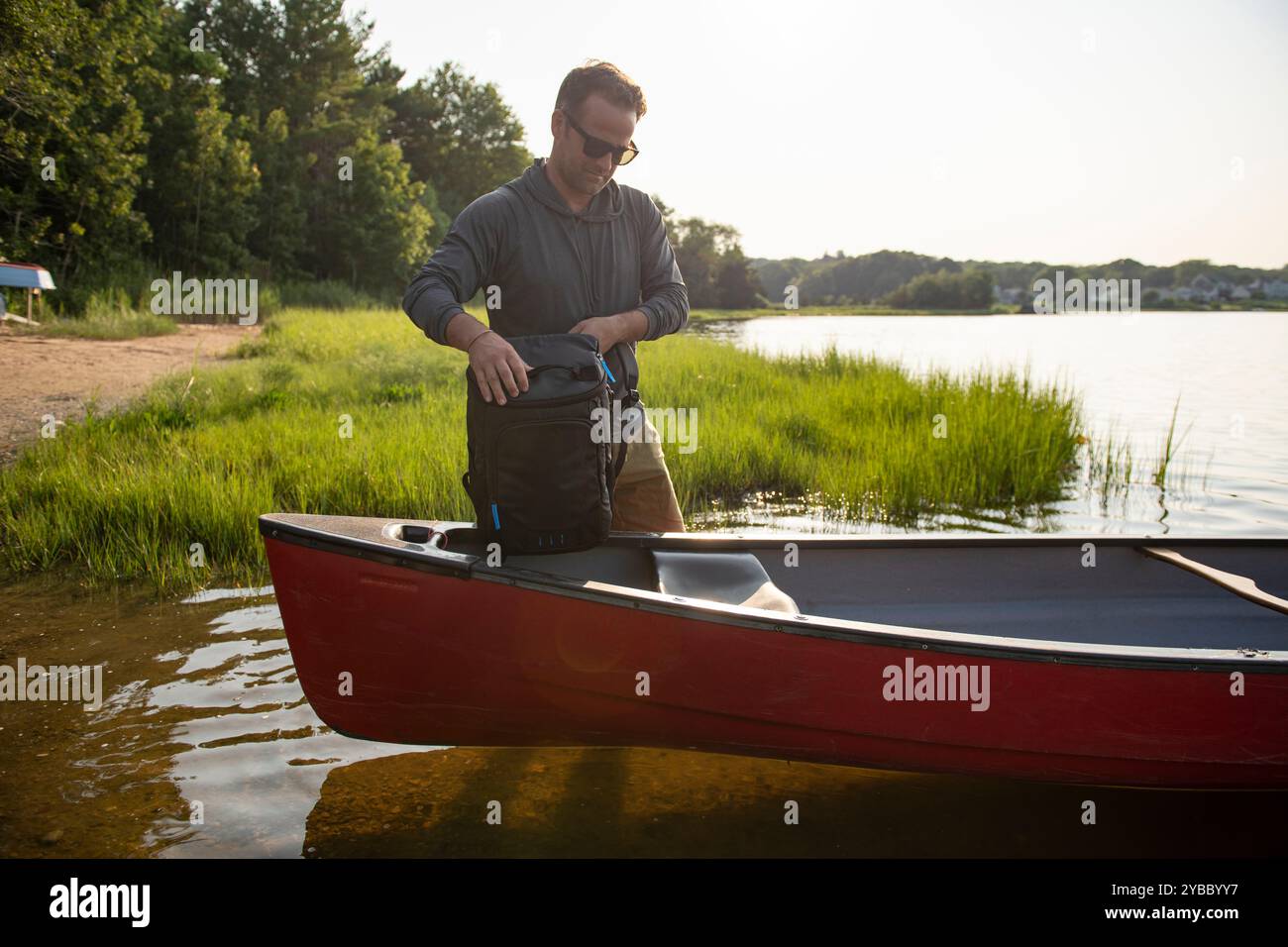 Man loading backpack into canoe on summer day Stock Photo - Alamy