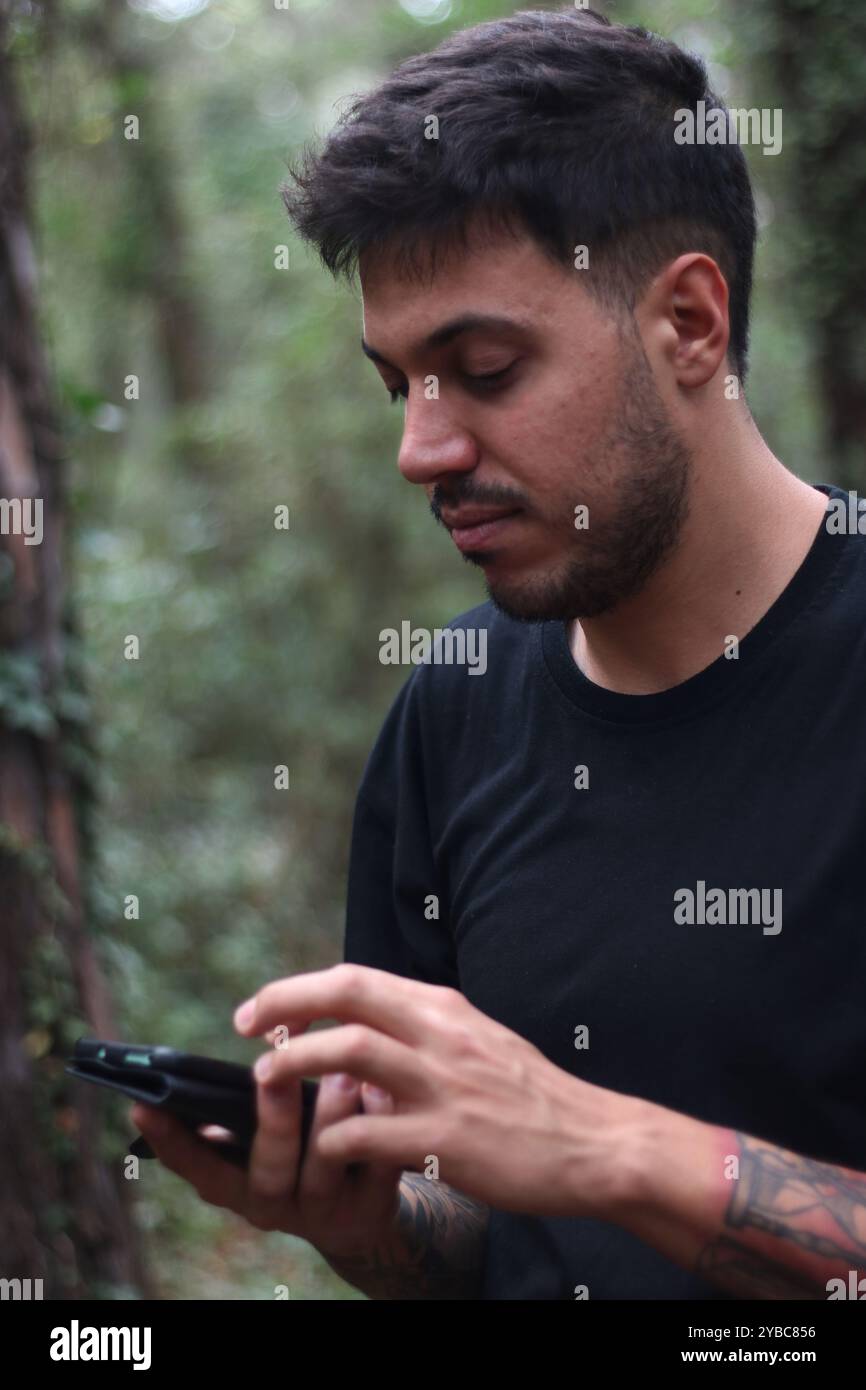 A young man stands in a peaceful forest, staring at his phone with a ...
