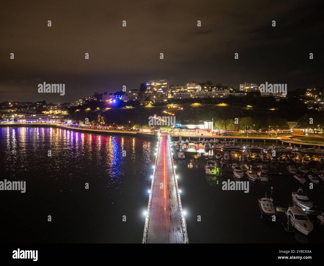 Aerial view of an illuminated pier leading to a seaside town at night ...