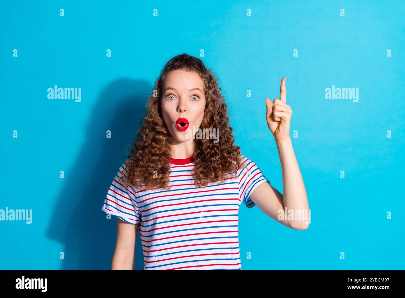 Surprised woman in striped shirt pointing upward with expression of ...