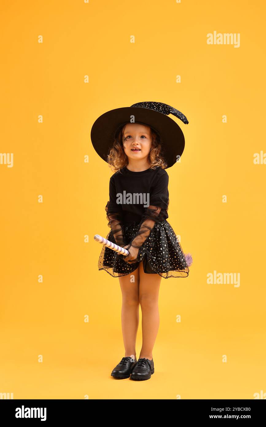 Cute girl with broom dressed like witch on yellow background. Halloween ...