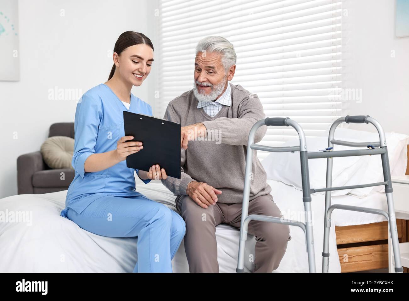 Doctor consulting senior patient with walking frame in hospital ward ...