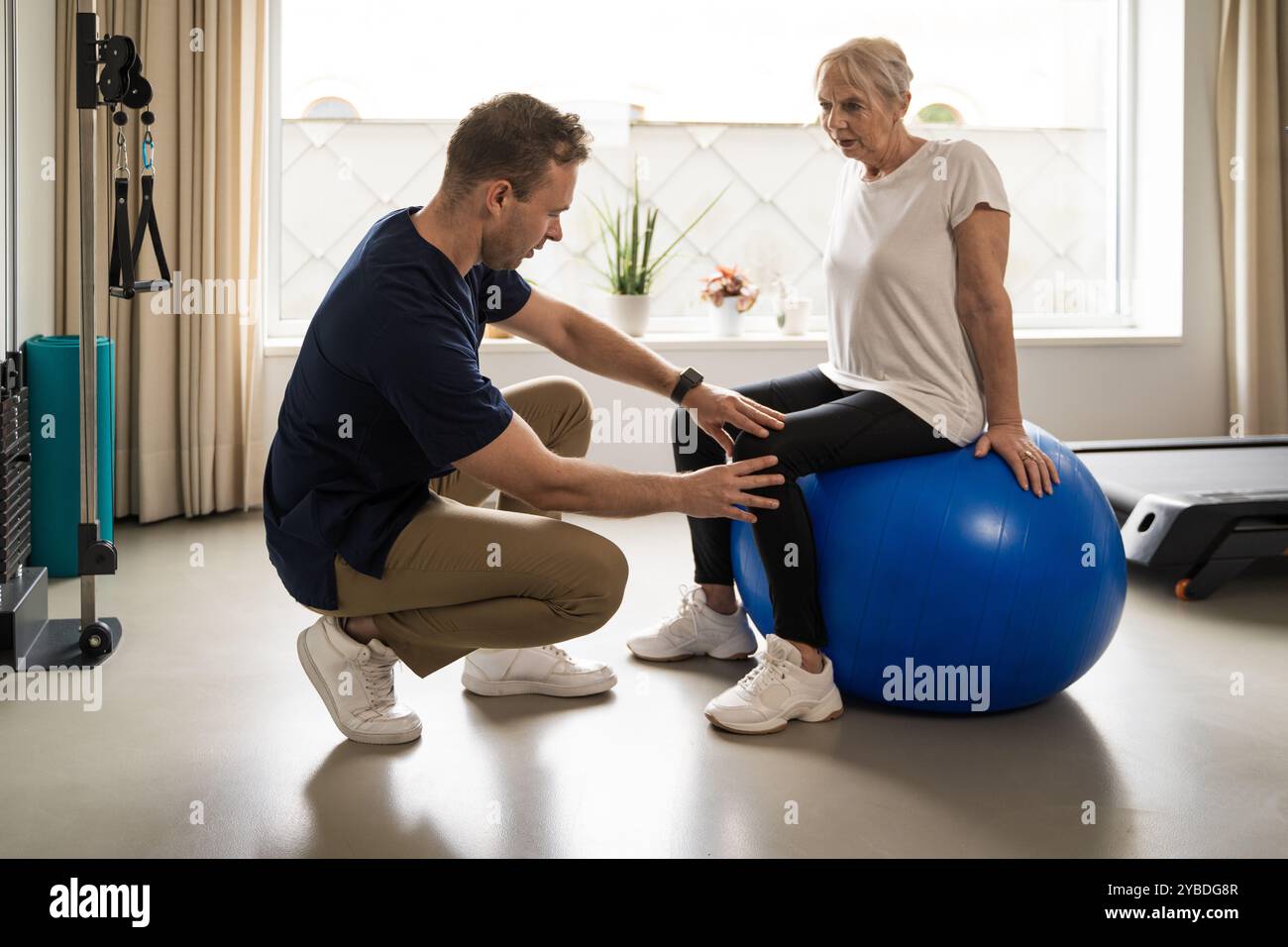 Male physiotherapist guiding elderly woman during stability ball ...