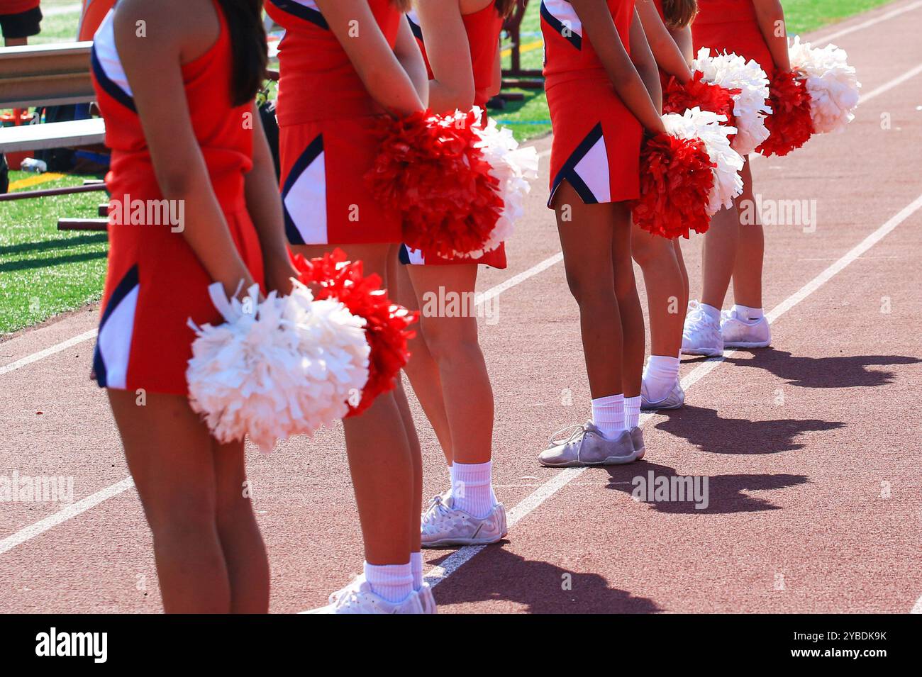 Rear view of high school cheerleaders holding their pom poms behind ...