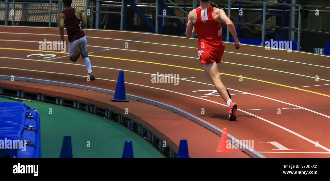 Two runners running in an indoor track relay race on a banked track ...