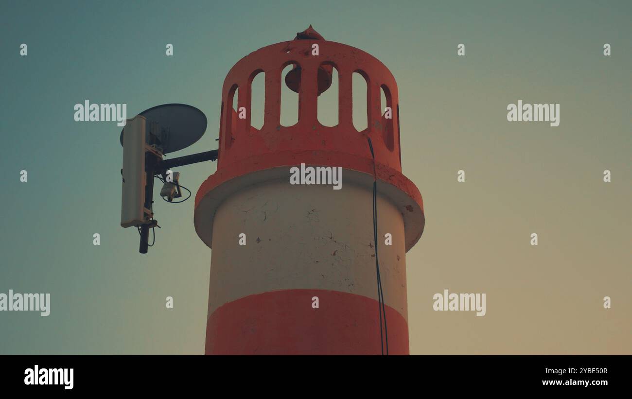 A lighthouse with a flashing lamp shows the way to passing ships. The ...