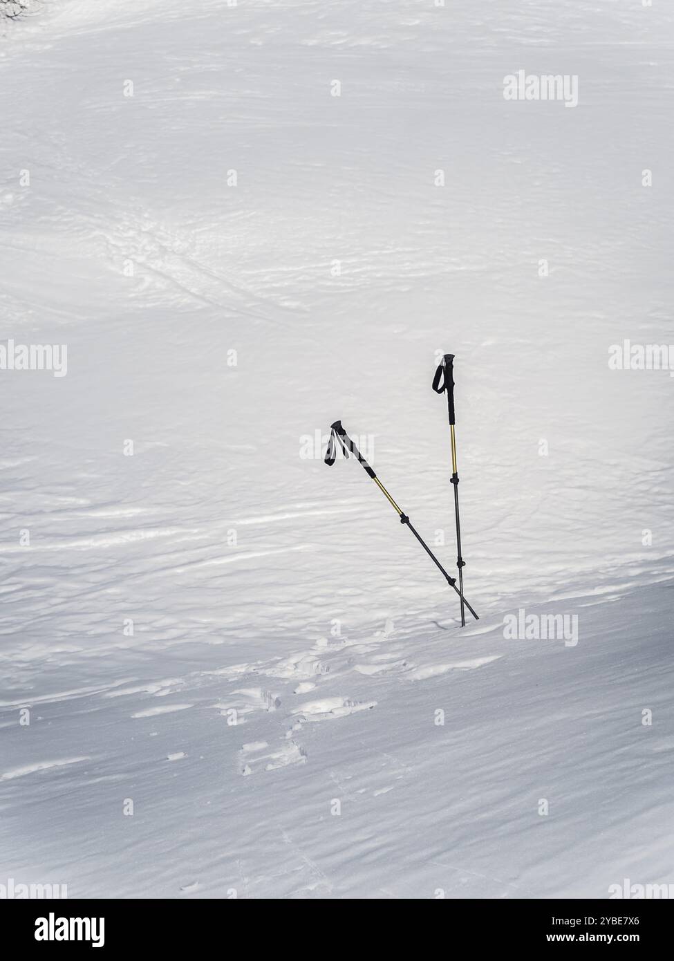 Two ski poles are stuck upright in fresh snow on a snowy slope, with ...
