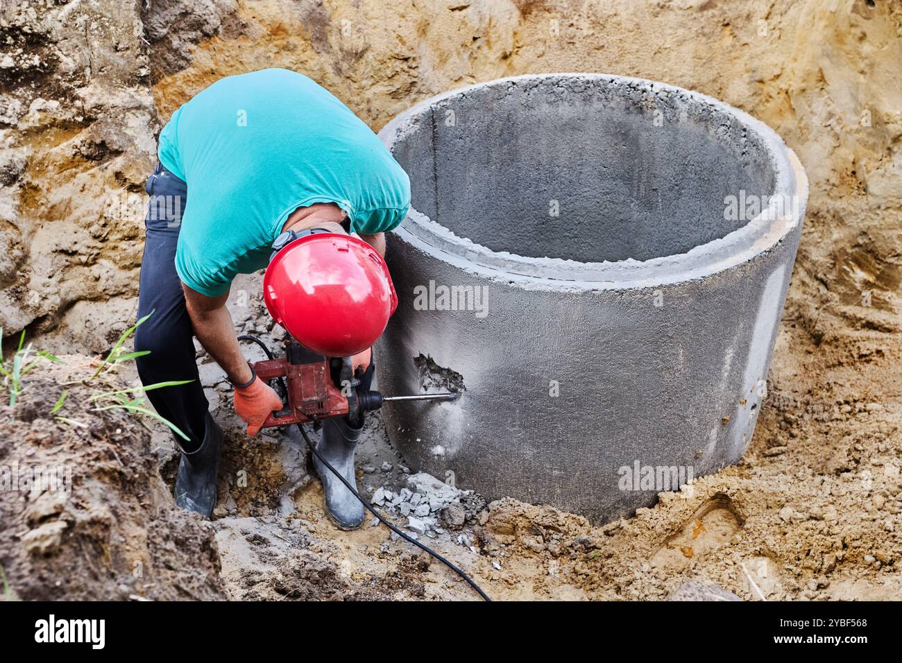 Worker chisels out hole for sewer pipe in concrete septic tank ring ...