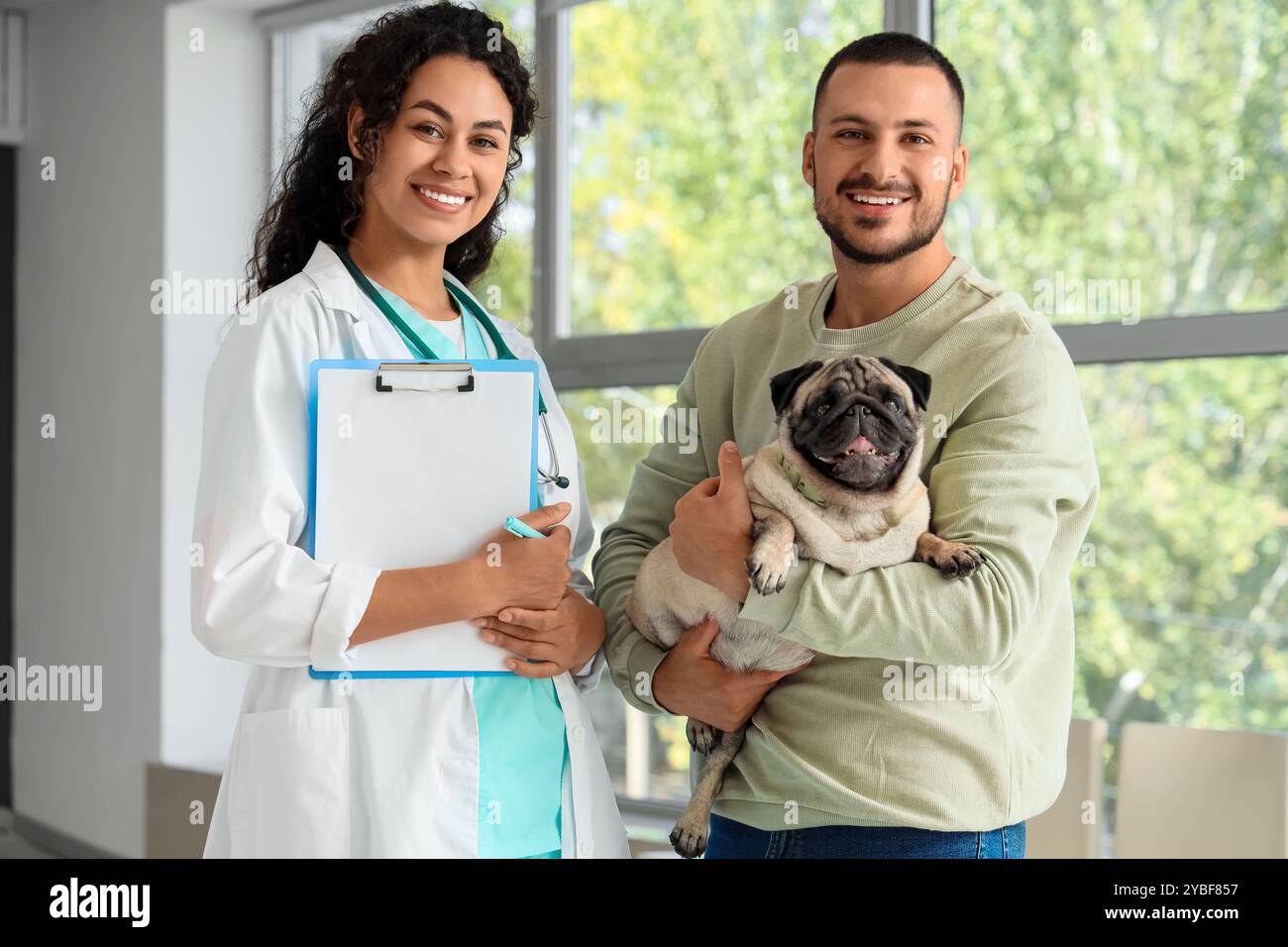 Female African-American veterinarian with owner and pug dog in hall of ...