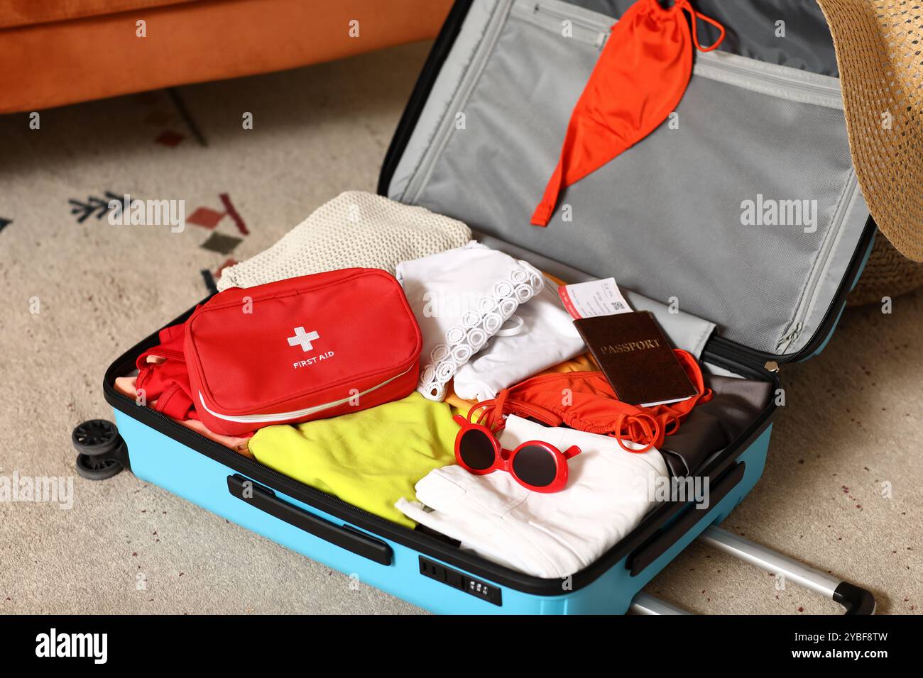 Suitcase with first aid kit, stylish clothes and passport on floor in ...