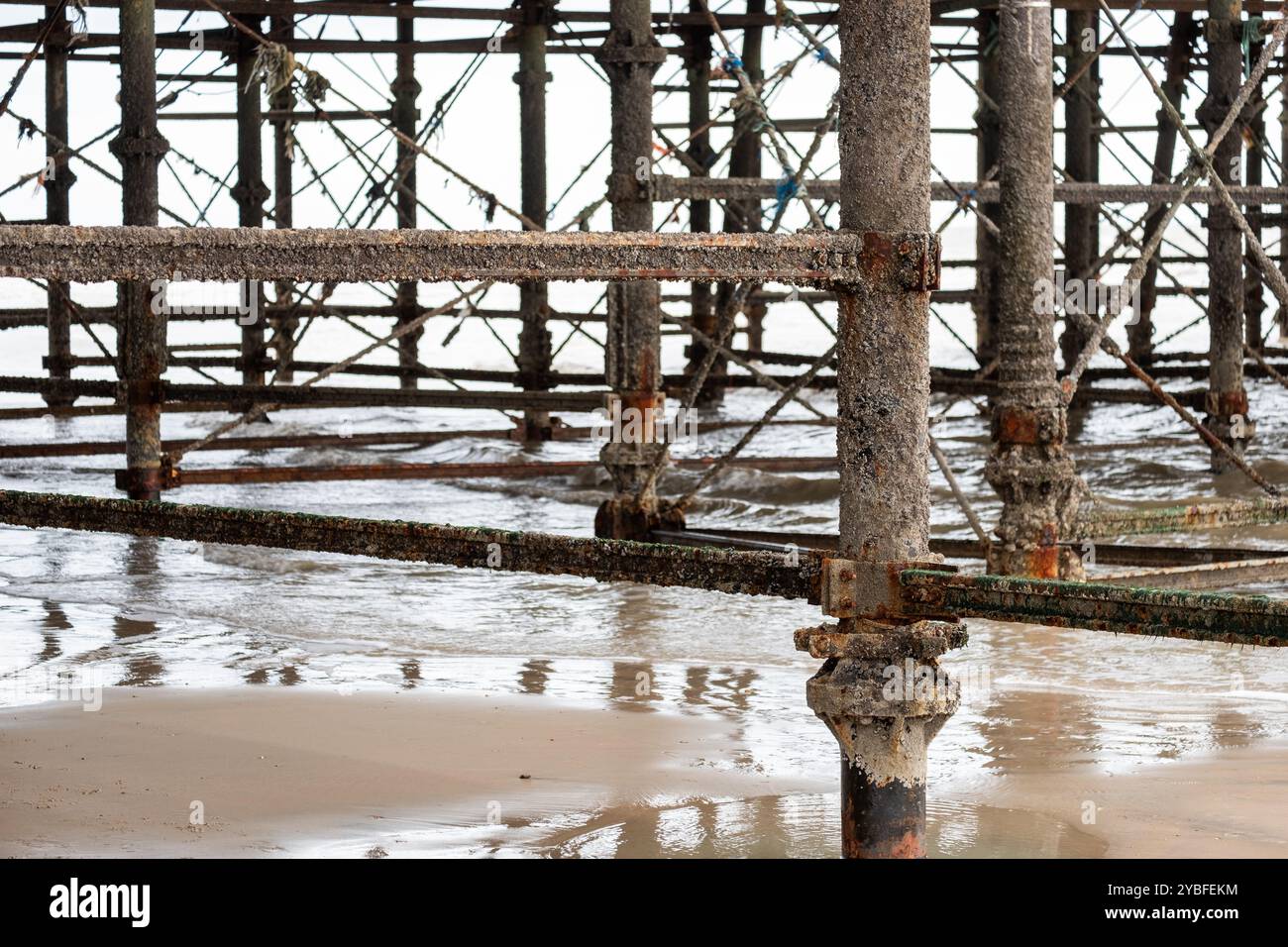 Multiple aged and rusted support beams are partially submerged in tranquil water beneath an old ...