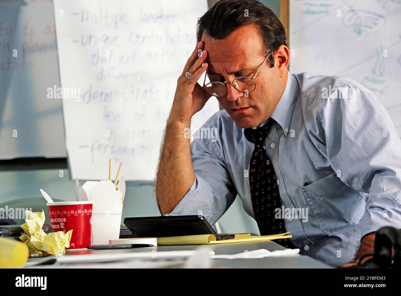 An office worker looks overwhelmed as he reviews documents and ...