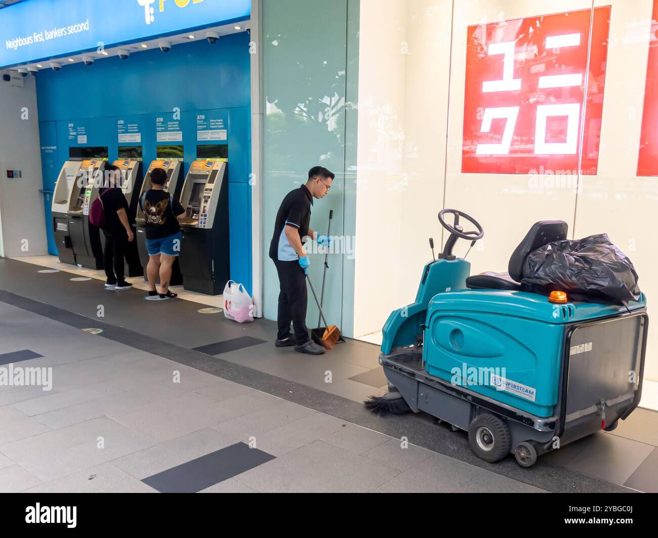 Women using ATM, Singapore. Street sweeper young man working, cleaning ...