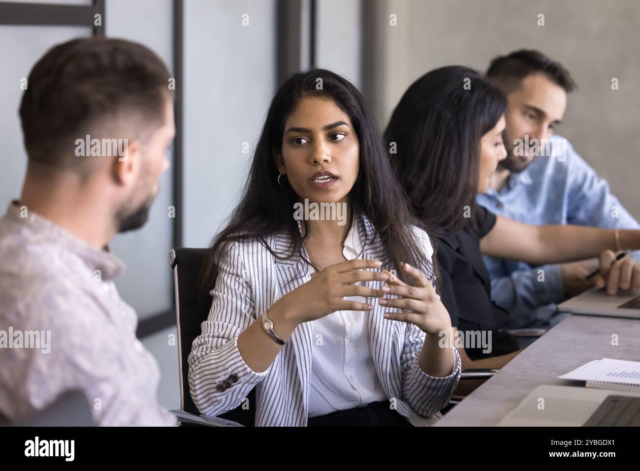 Serious beautiful young Indian professional woman talking to colleague ...