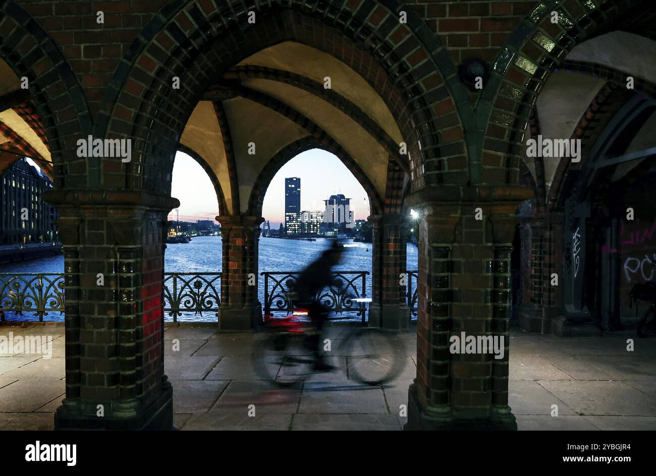 Bicycle rider to the sunrise at the Oberbaum Bridge, view through the arcades over the Spree to ...