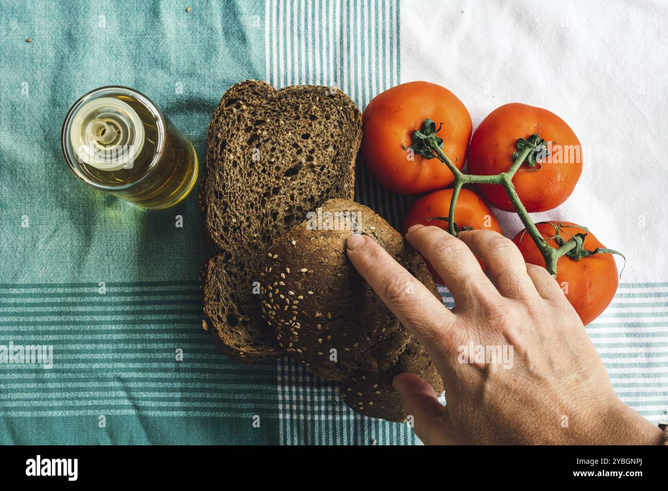 Hand over on Olive oil, tomato and slides of brown bread on tablecloth ...