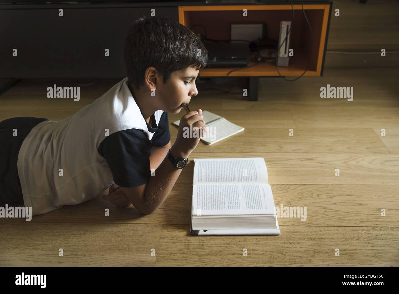 Little boy child reading a book. He lies on the floor. Side view ...